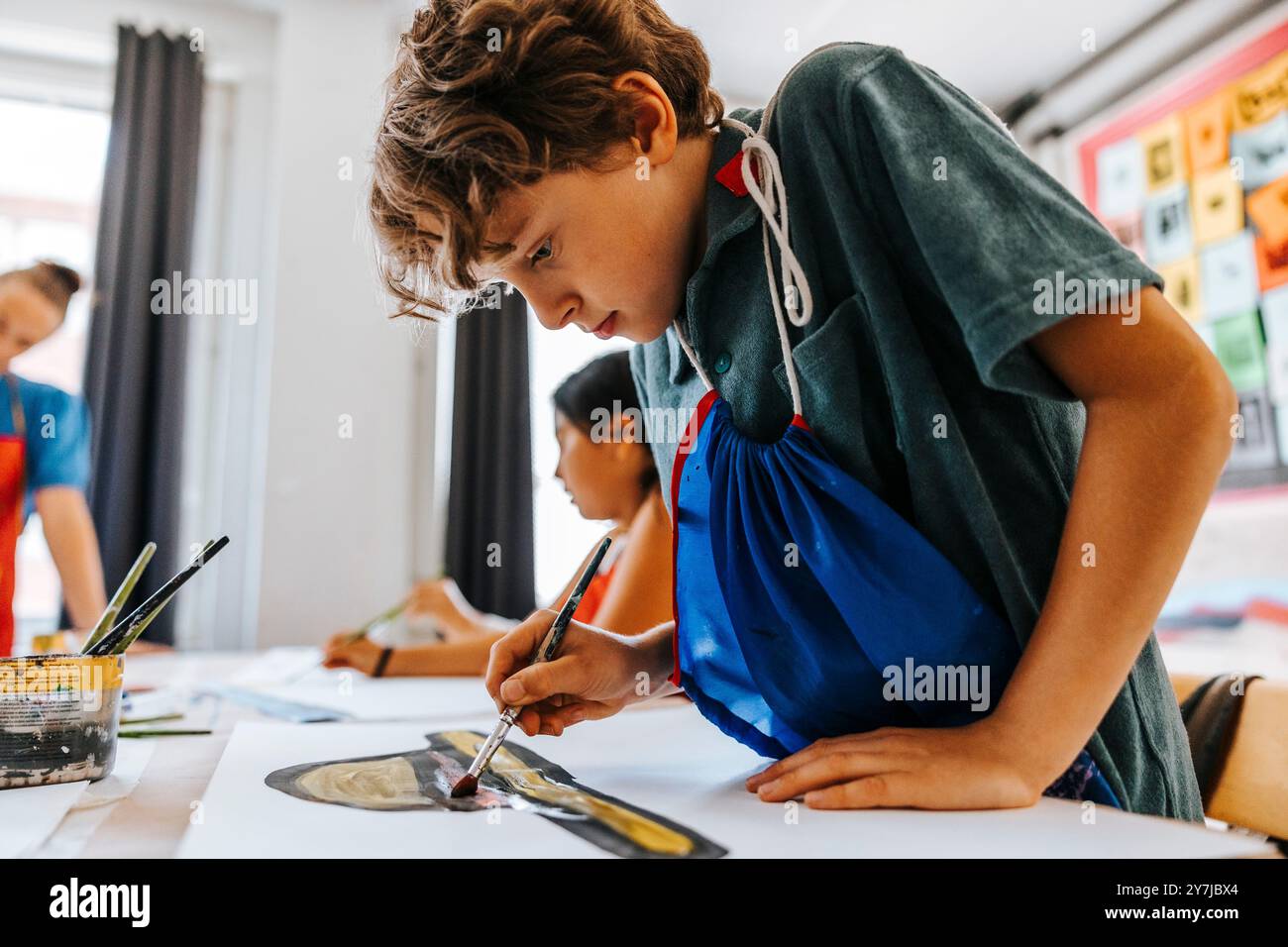 Focused boy painting with paintbrush on paper during art class at ...