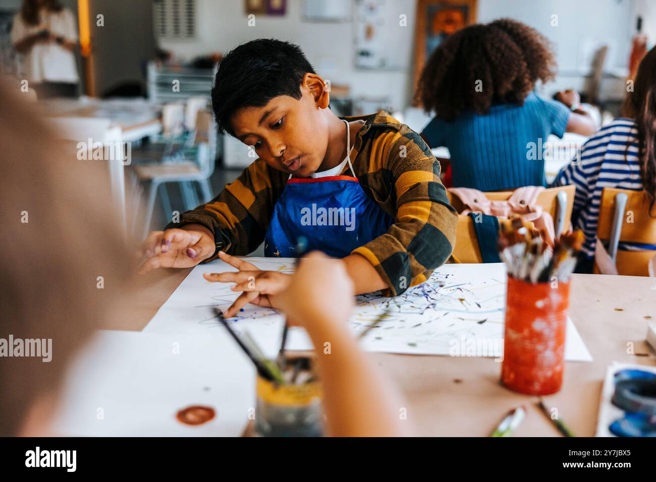 Boy doing finger painting on paper during art class at elementary ...