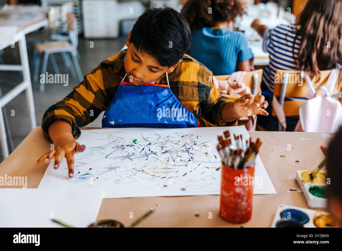 Focused boy doing finger painting on paper during art class at ...