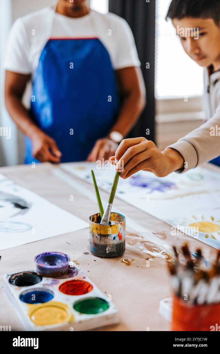 Boy dipping paintbrush in water during art class at elementary school ...