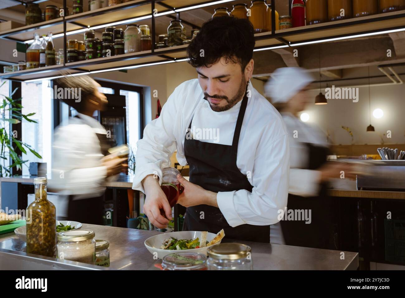 Male chef pouring oil in salad bowl while standing in commercial ...