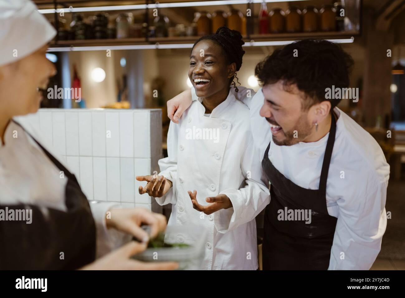 Cheerful male chef with arm around female colleague enjoying at ...