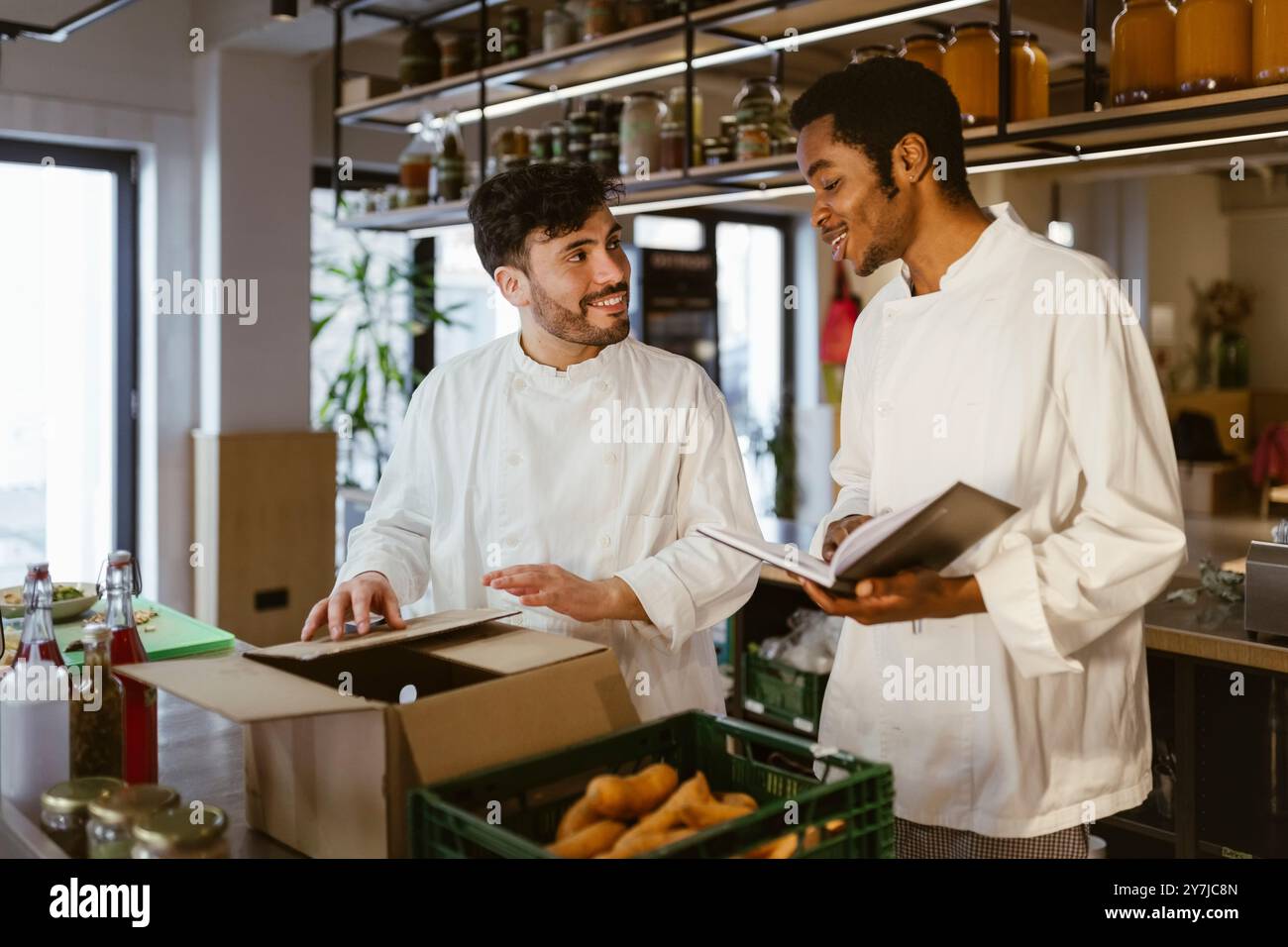 Smiling young chef holding book and taking inventory with male ...