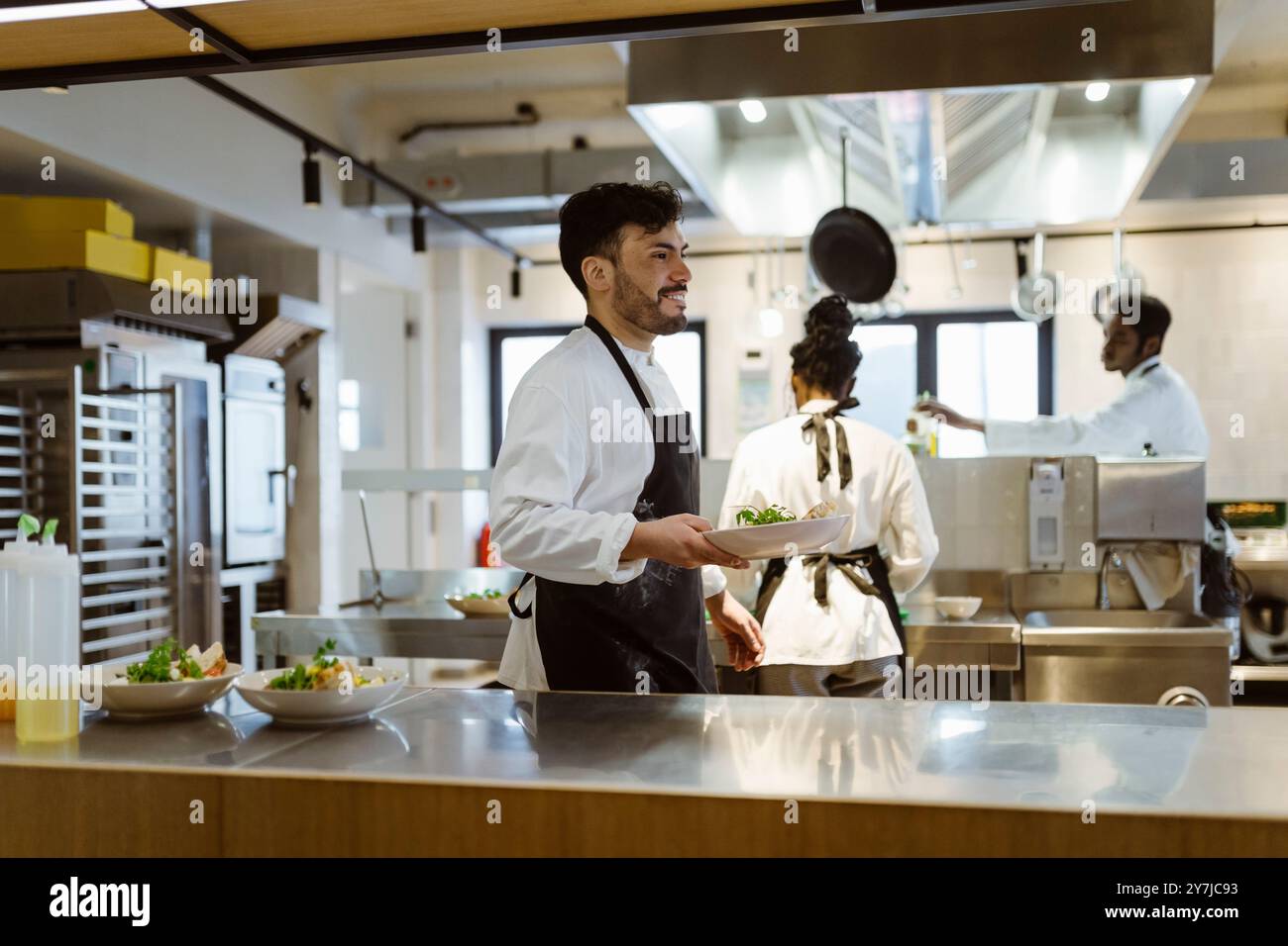 Smiling male chef holding salad bowl and walking near kitchen counter ...