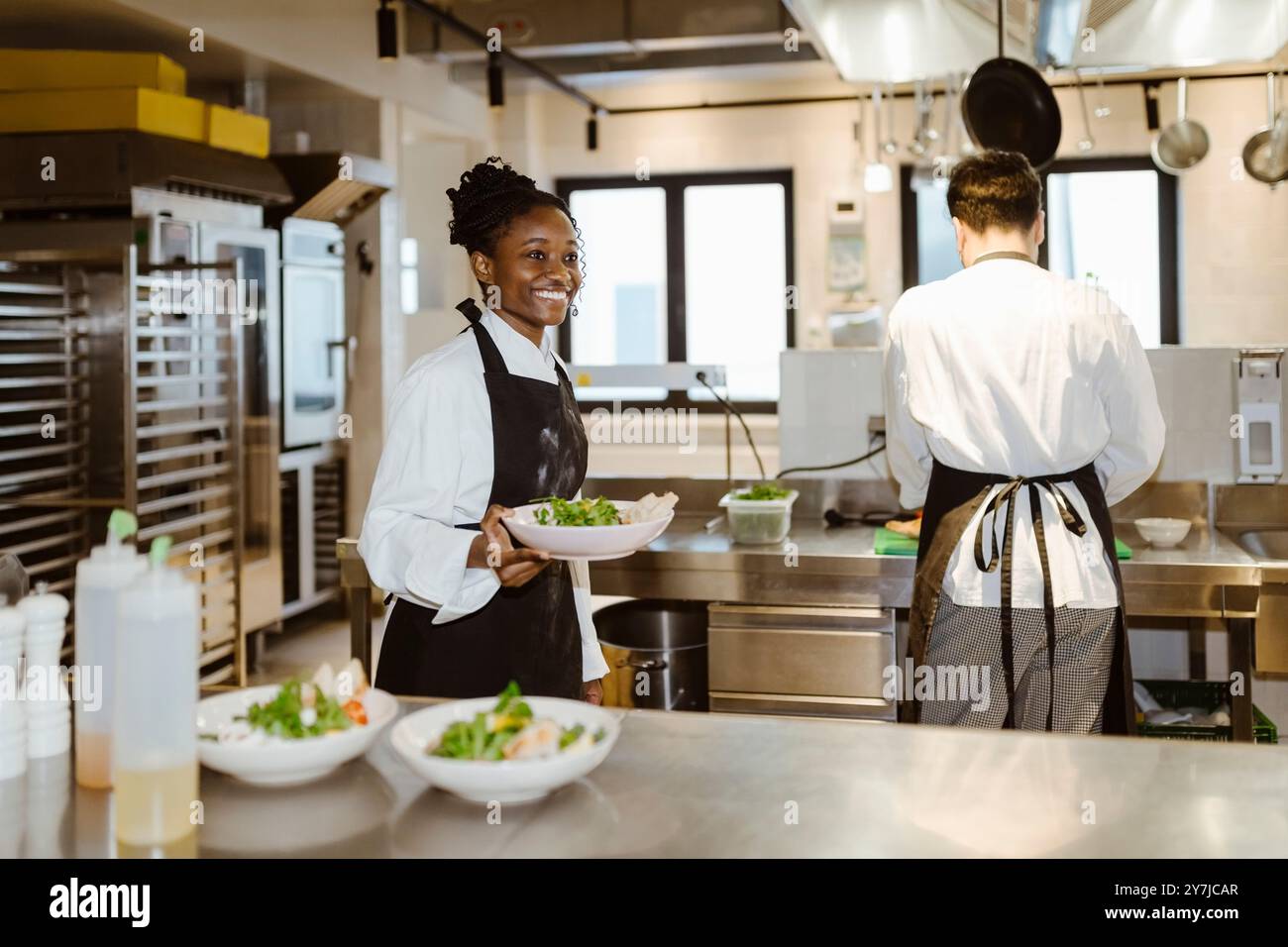 Smiling young chef walking with salad bowl in commercial kitchen at ...