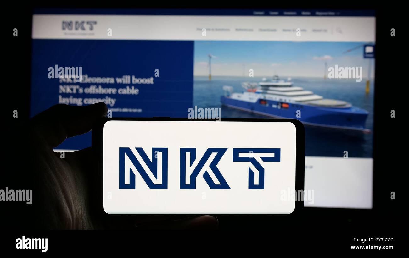 Person holding smartphone with logo of Danish voltage cable company NKT ...
