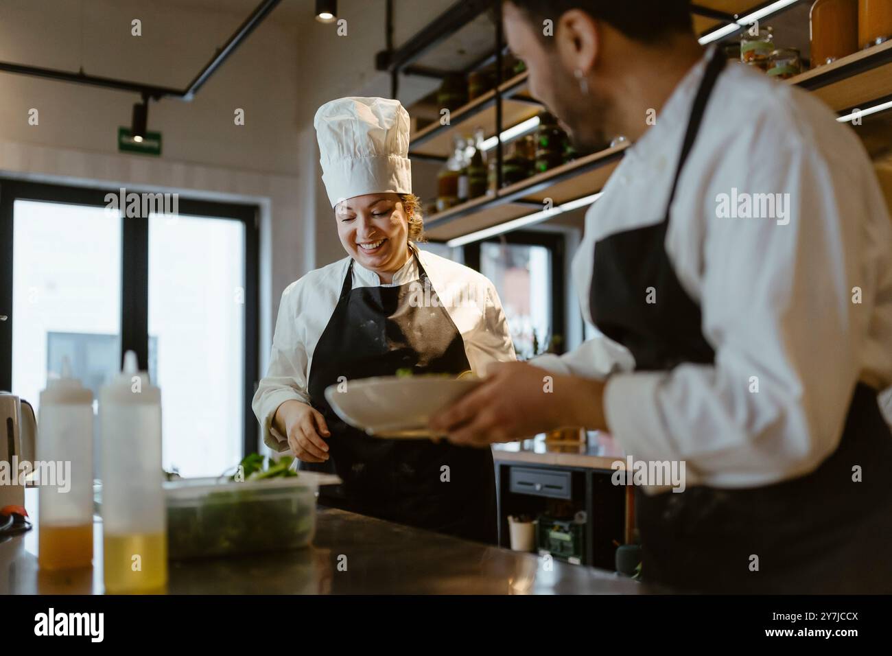 Smiling female chef working with male colleague in commercial kitchen ...