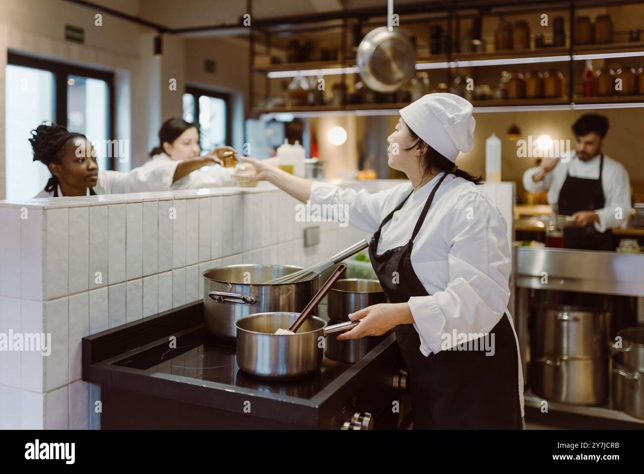 Young chef passing ingredient to female chef preparing food in ...