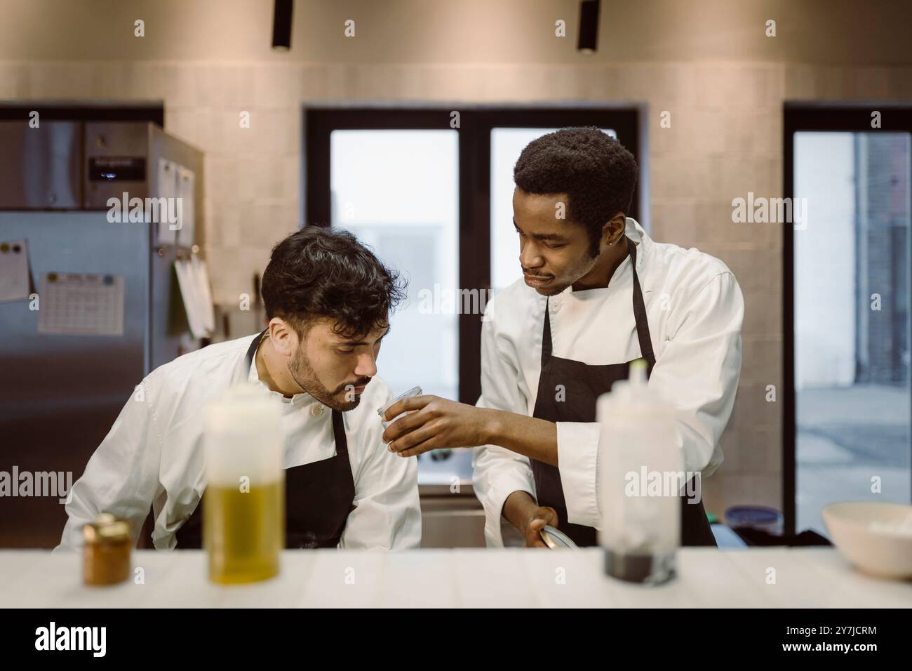 Young male chef with colleague smelling ingredient in commercial ...