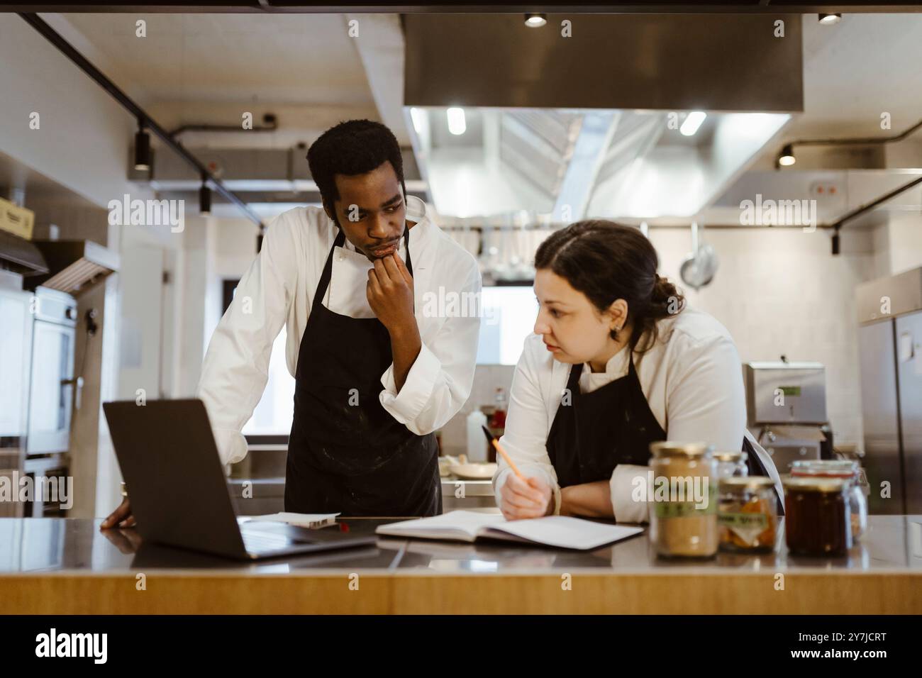 Female chef leaning on counter while discussing with male colleague in ...