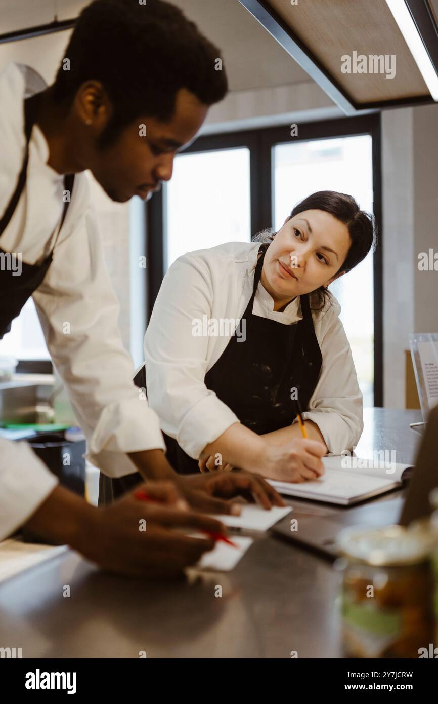 Male chef discussing with female colleague leaning on counter in ...