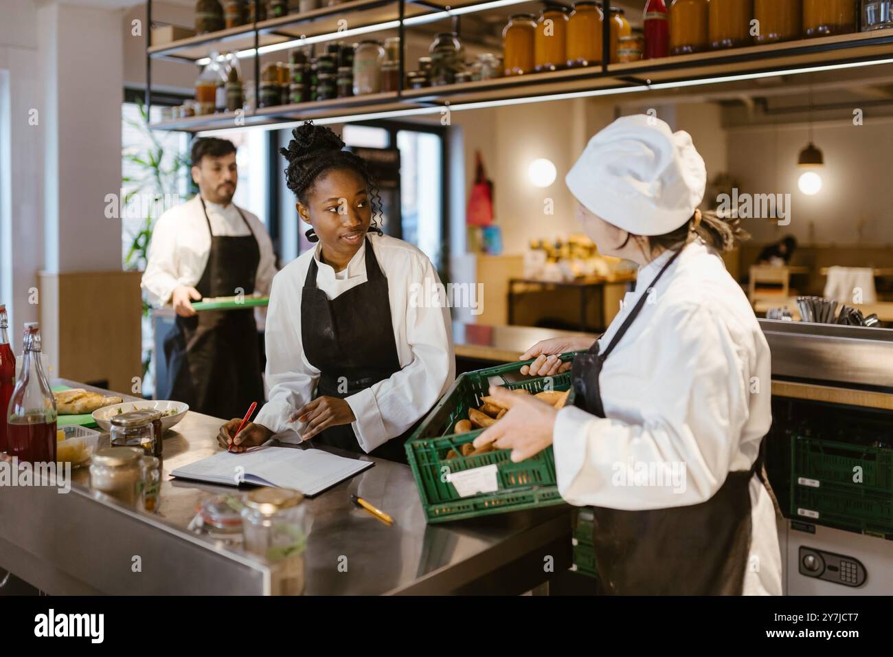 Female chef holding crate and taking inventory with colleague in ...