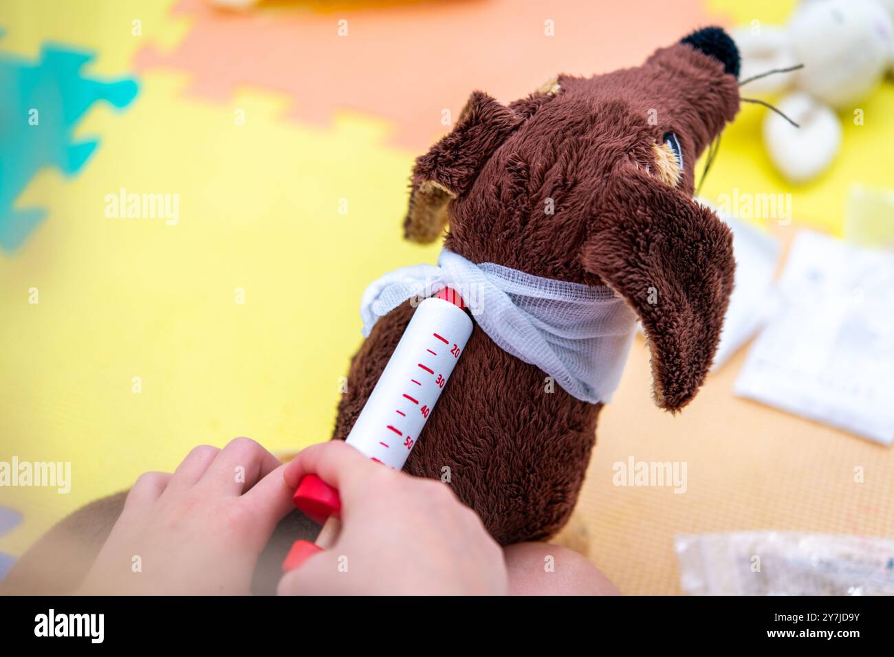 A child cares for a stuffed dog with a syringe, simulating pet ...