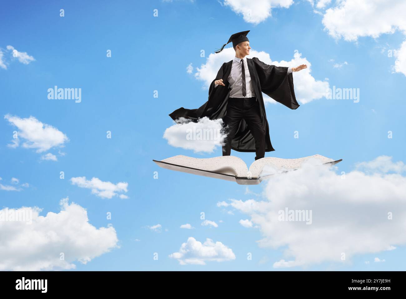 Male graduate student standing on a book and flying high up in the sky ...