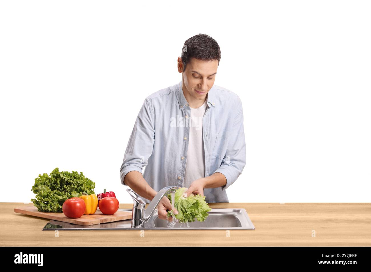 Young man washing vegetables in a sink isolated on white background ...