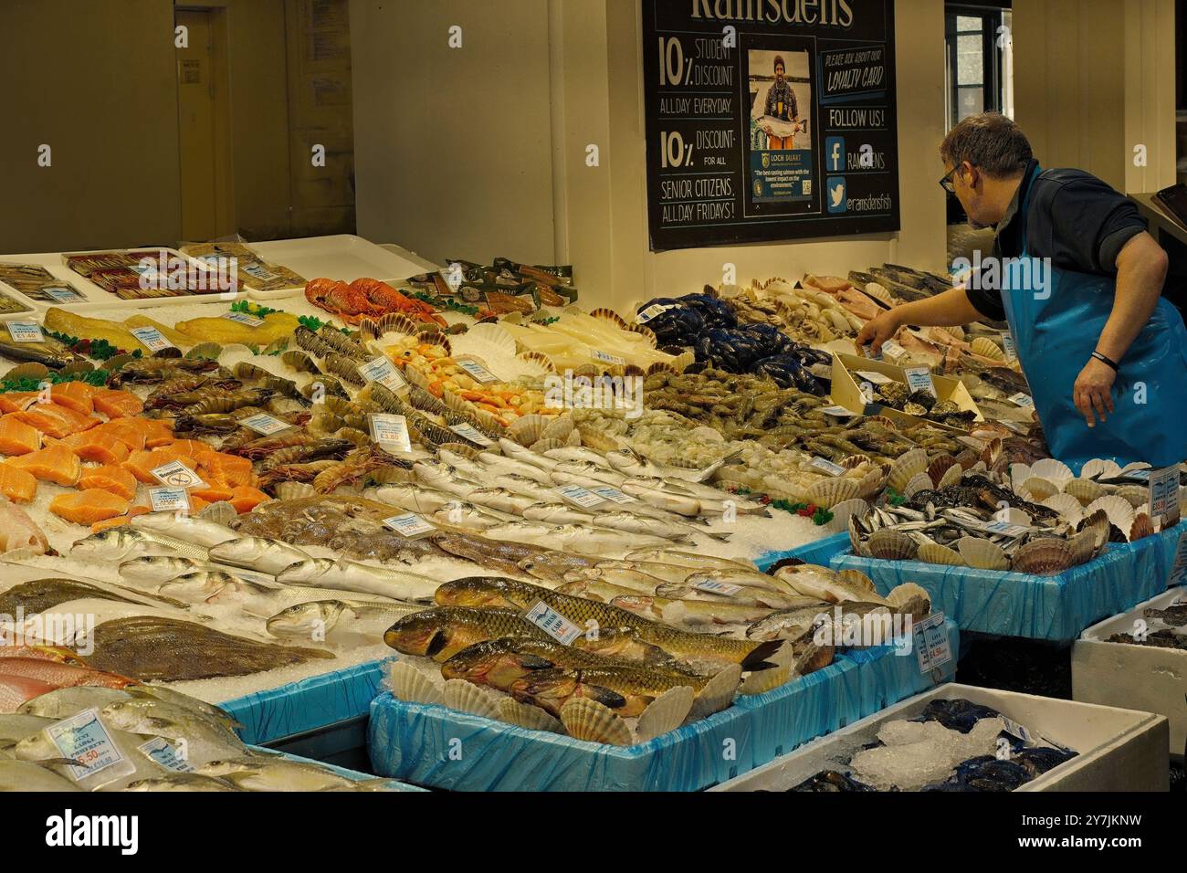 An apron-clad man works through a display of fresh fish and seafood at ...