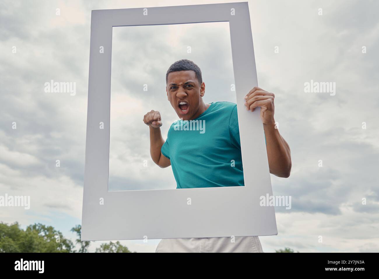 Furious mixed race man looking through a picture frame and gesturing ...