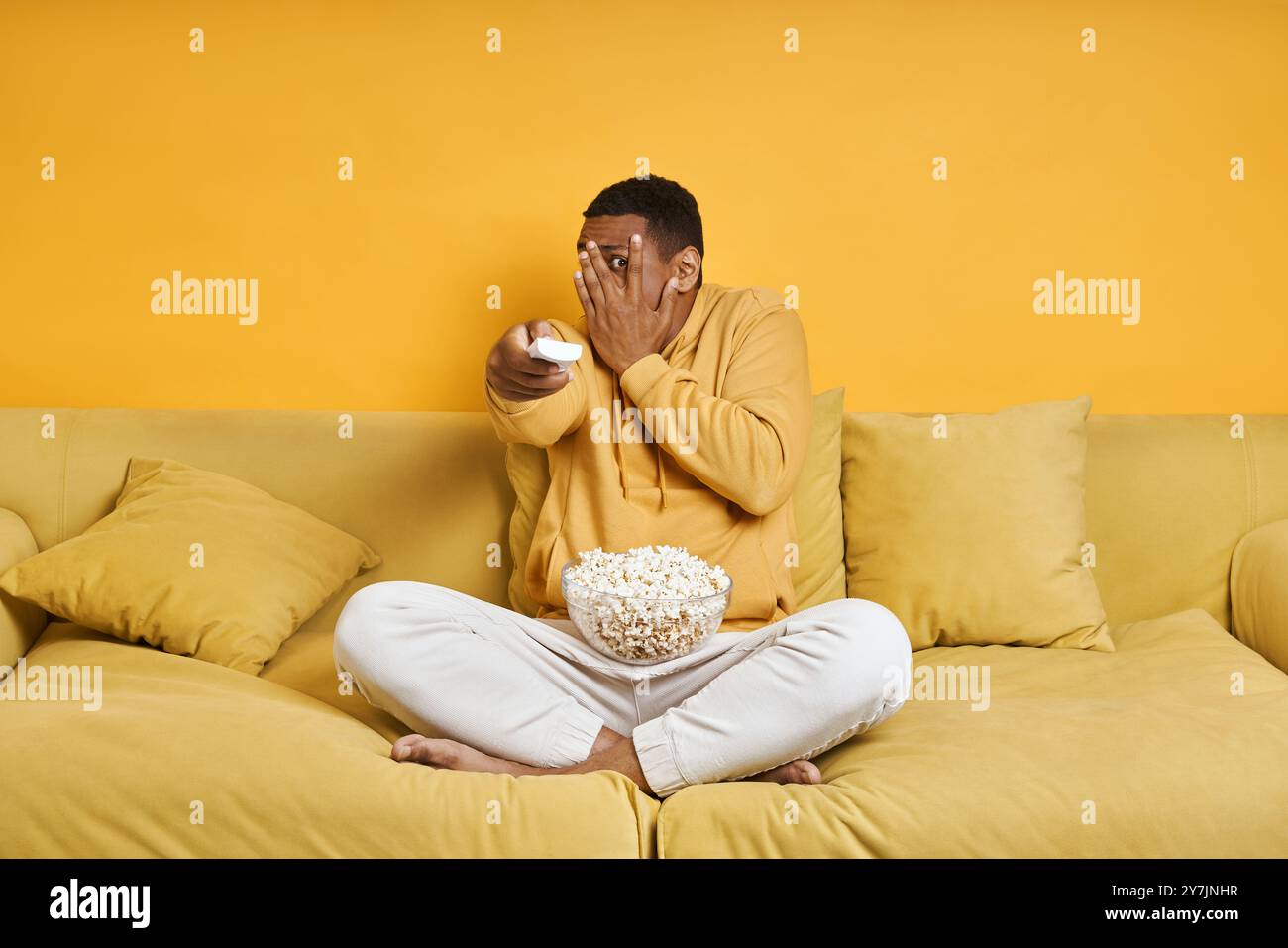 Young man watching TV and looking terrified while sitting on the couch ...