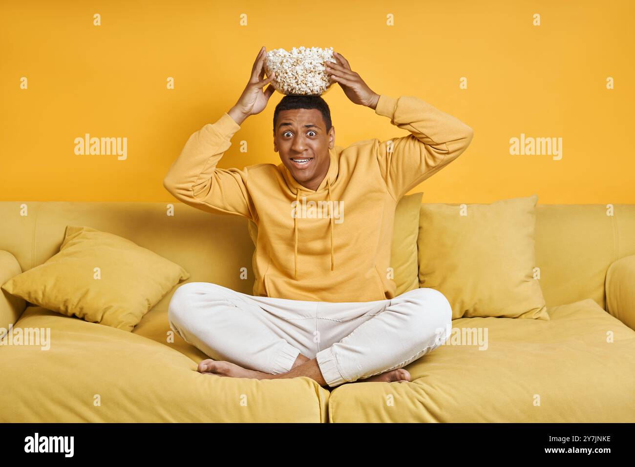 Playful man carrying plate with popcorn on head while relaxing on the ...