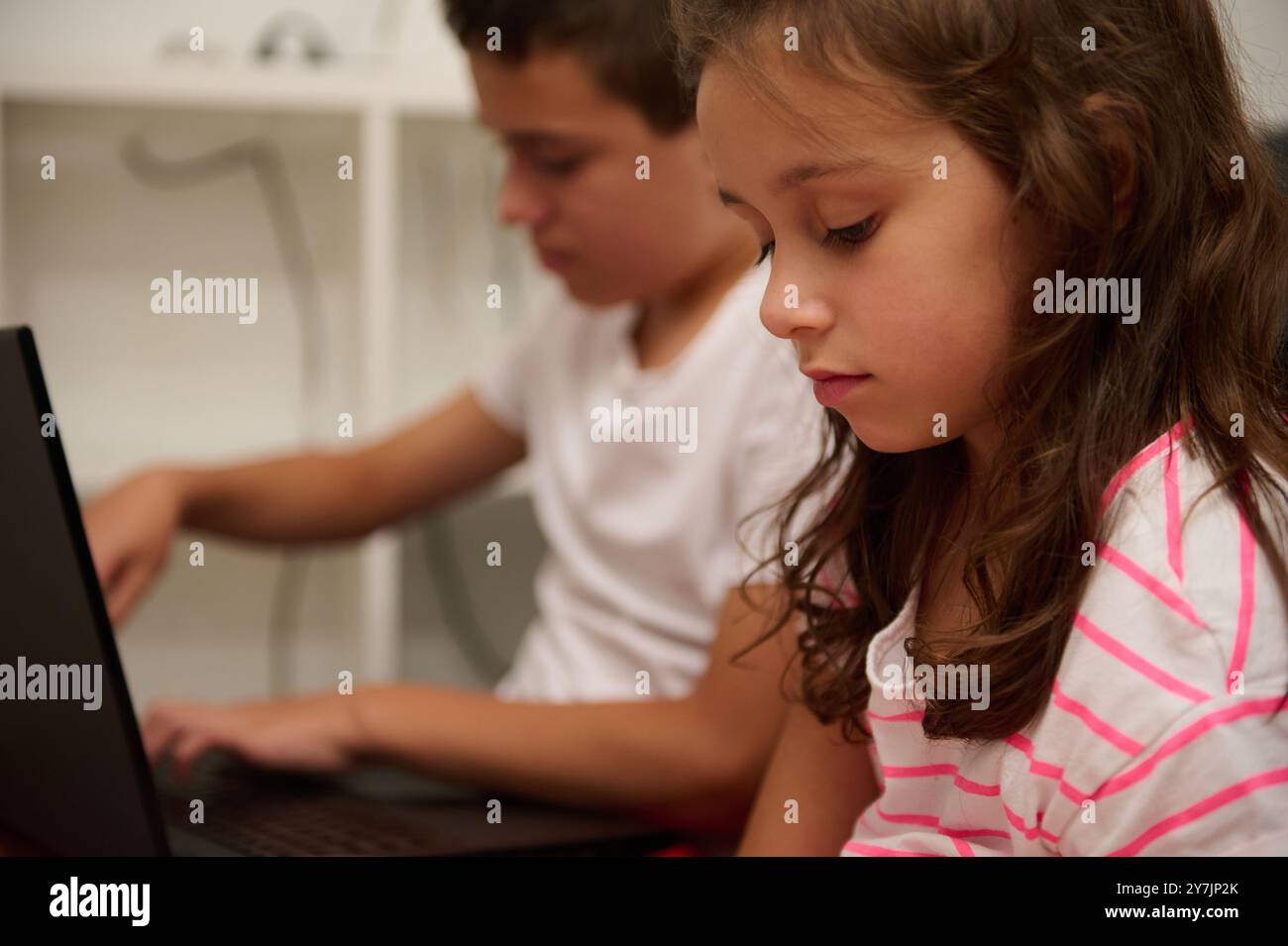 Two children are intently using laptops for online learning. The close ...