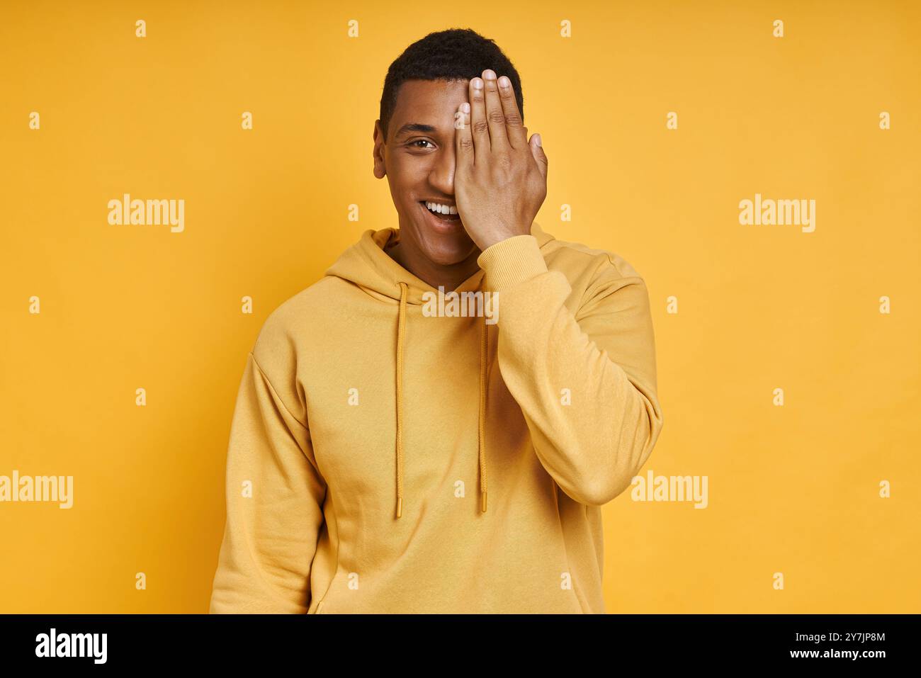 Playful mixed race man covering half face with hand while standing ...