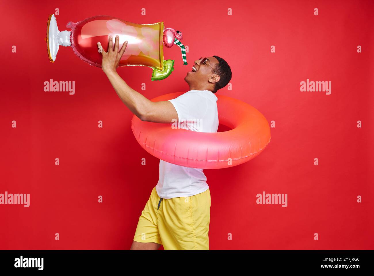 Playful young man carrying inflatable ring and cocktail while standing ...