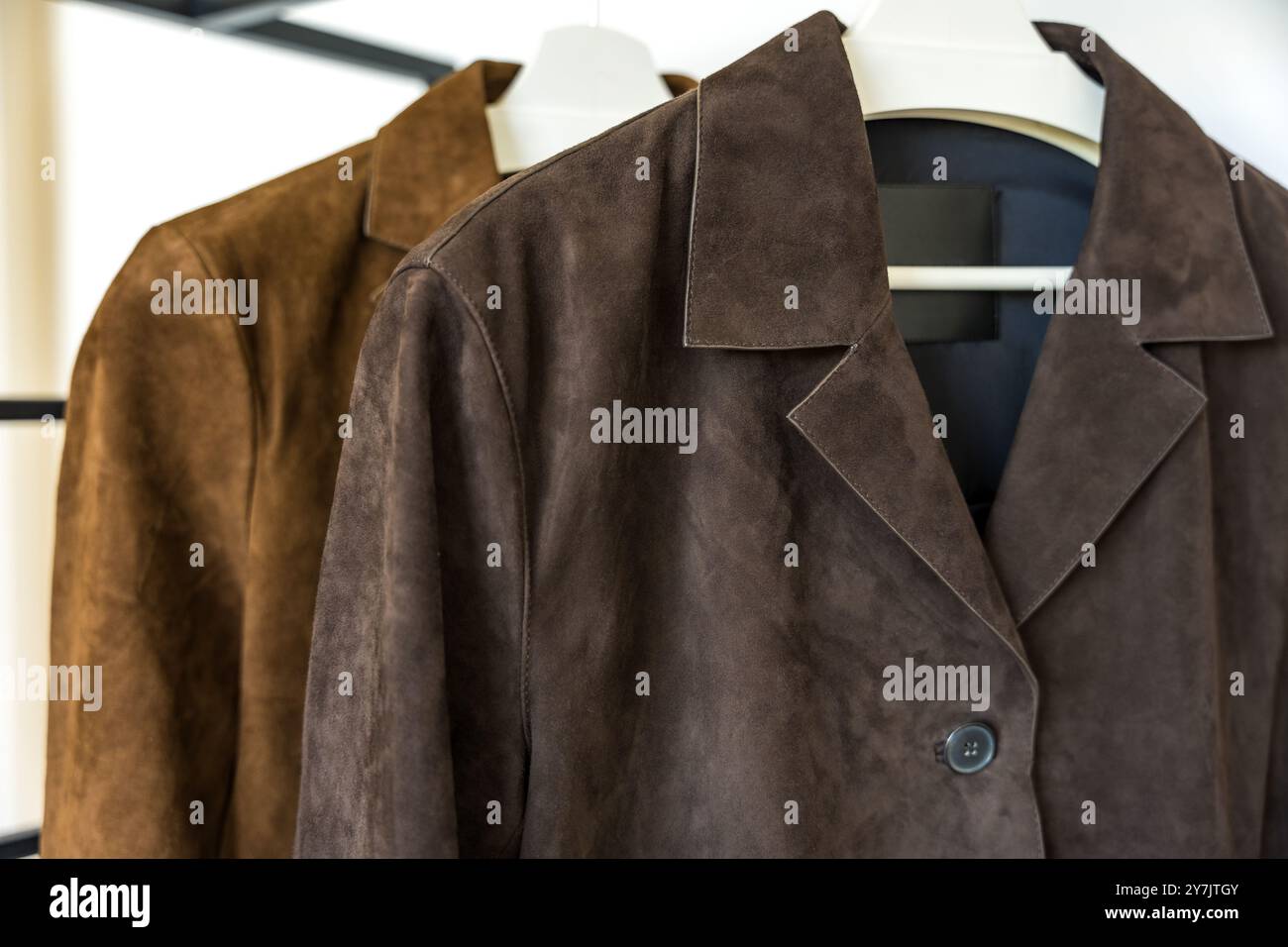 Two brown natural suede jackets of different shades hanging on a hanger ...