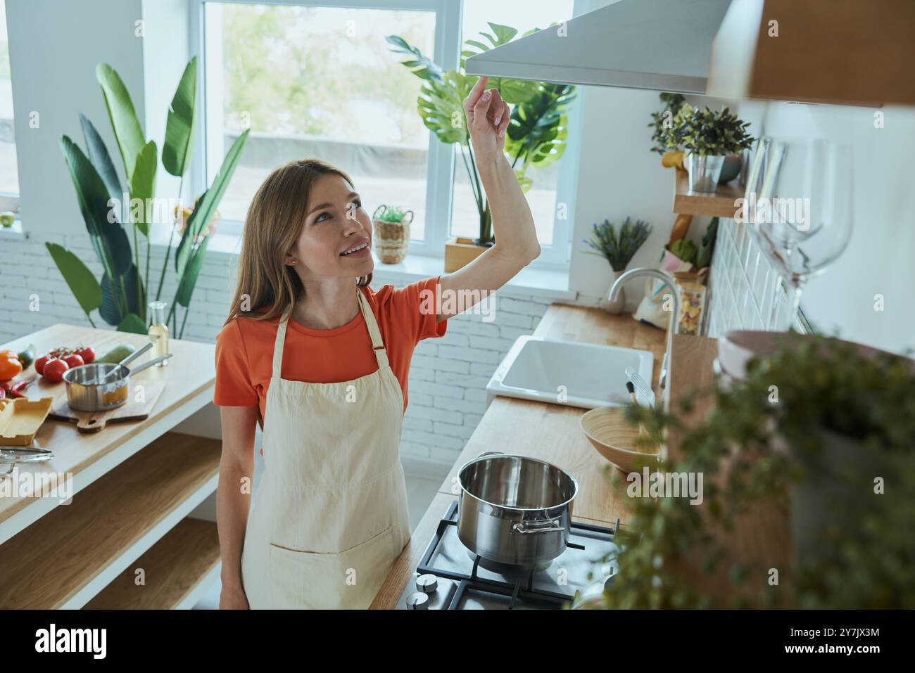 Top view of confident young woman turning on a cooking hood while ...