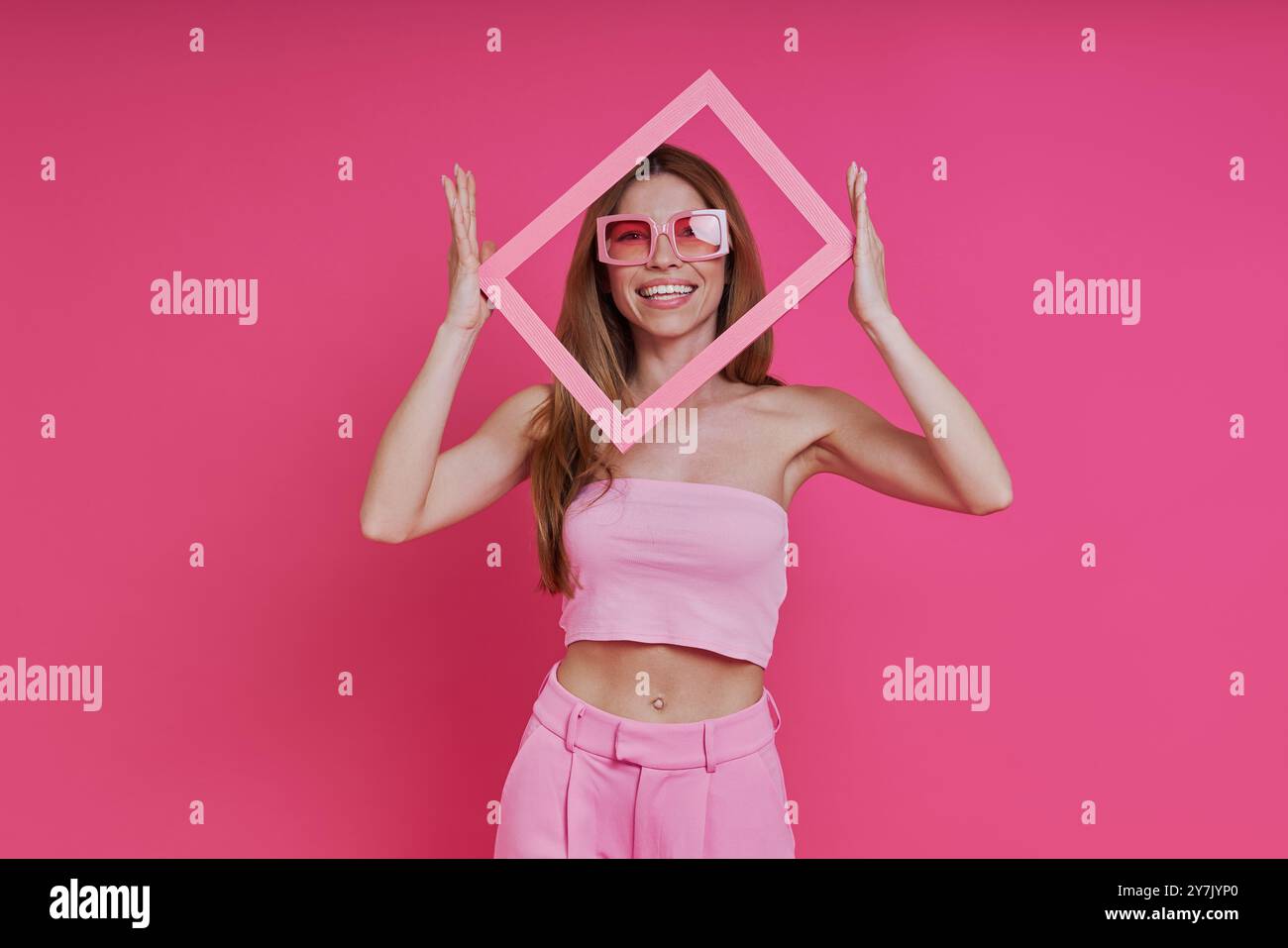 Excited young woman looking through a picture frame while standing ...