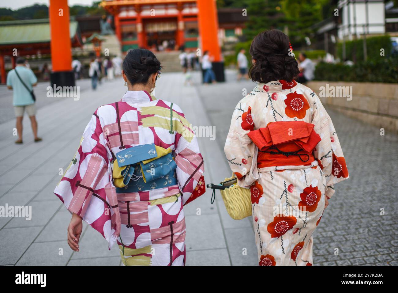 Two young women wearing traditional Japanese clothes and the torii gate ...