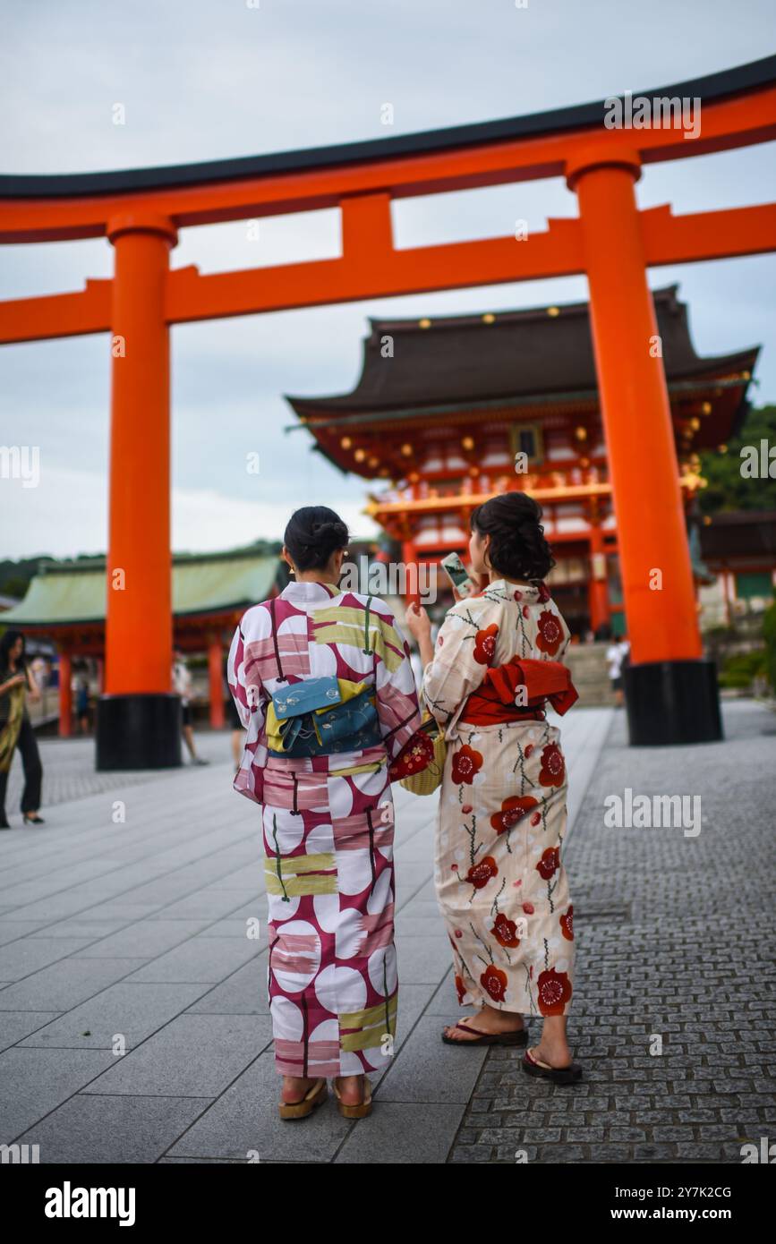 Two young women wearing traditional Japanese clothes and the torii gate ...