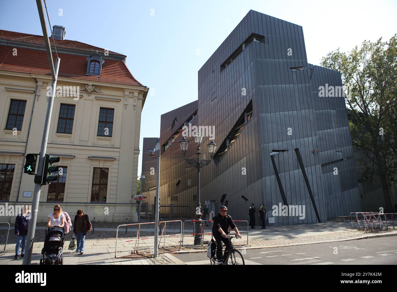Woman & stroller, man rides a bike crossing street in front of the two building Jewish Museum ...