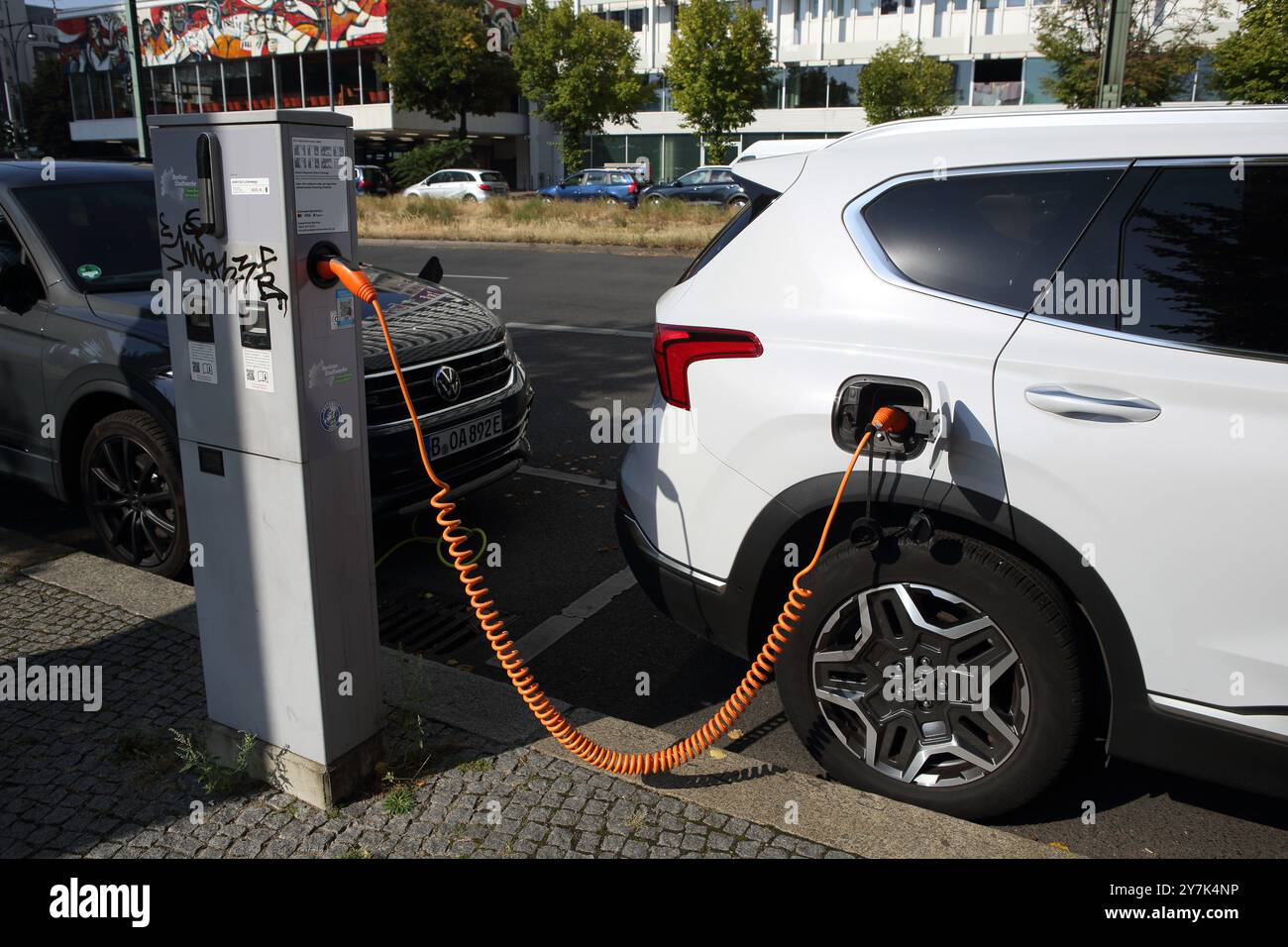 White electric car being charged with a cable plugged in it's back side ...