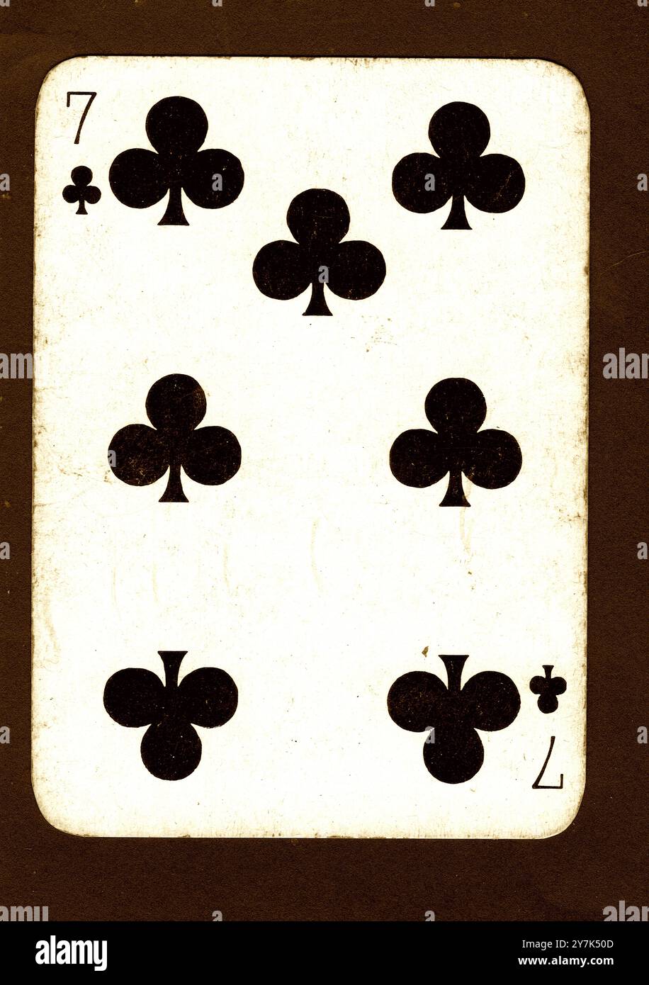 A vintage seven of clubs playing card in sepia on a black background ...