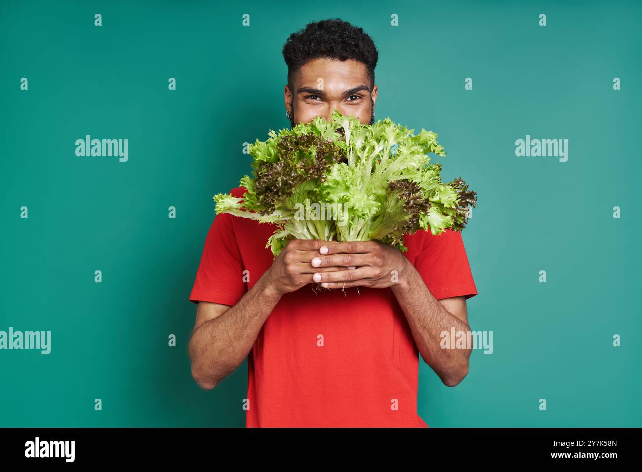 Playful African man hiding face behind a bunch of lettuce while ...