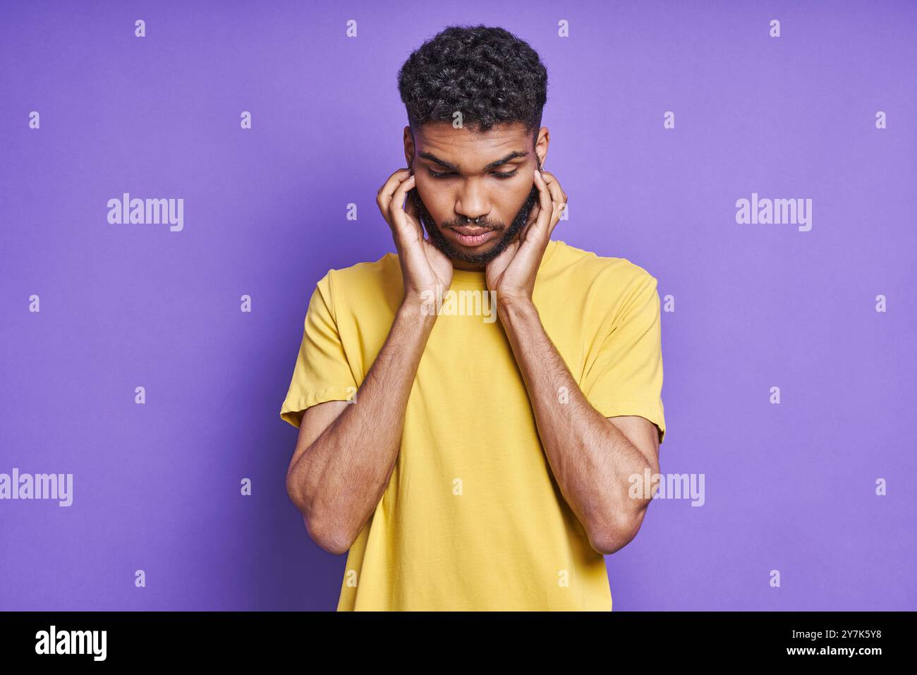 Frustrated African man touching face while standing against purple ...