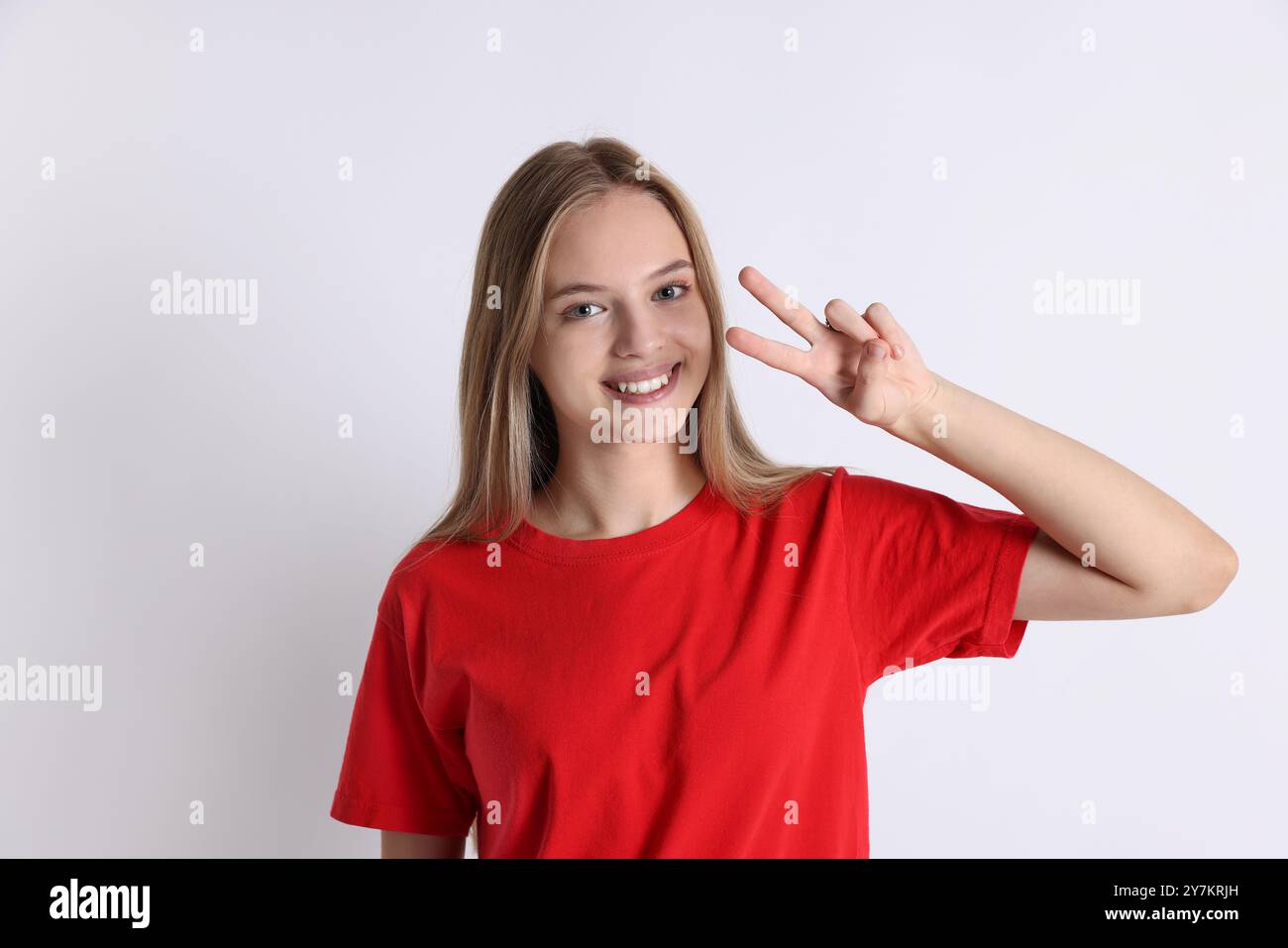Teenage girl showing v-sign on white background Stock Photo - Alamy