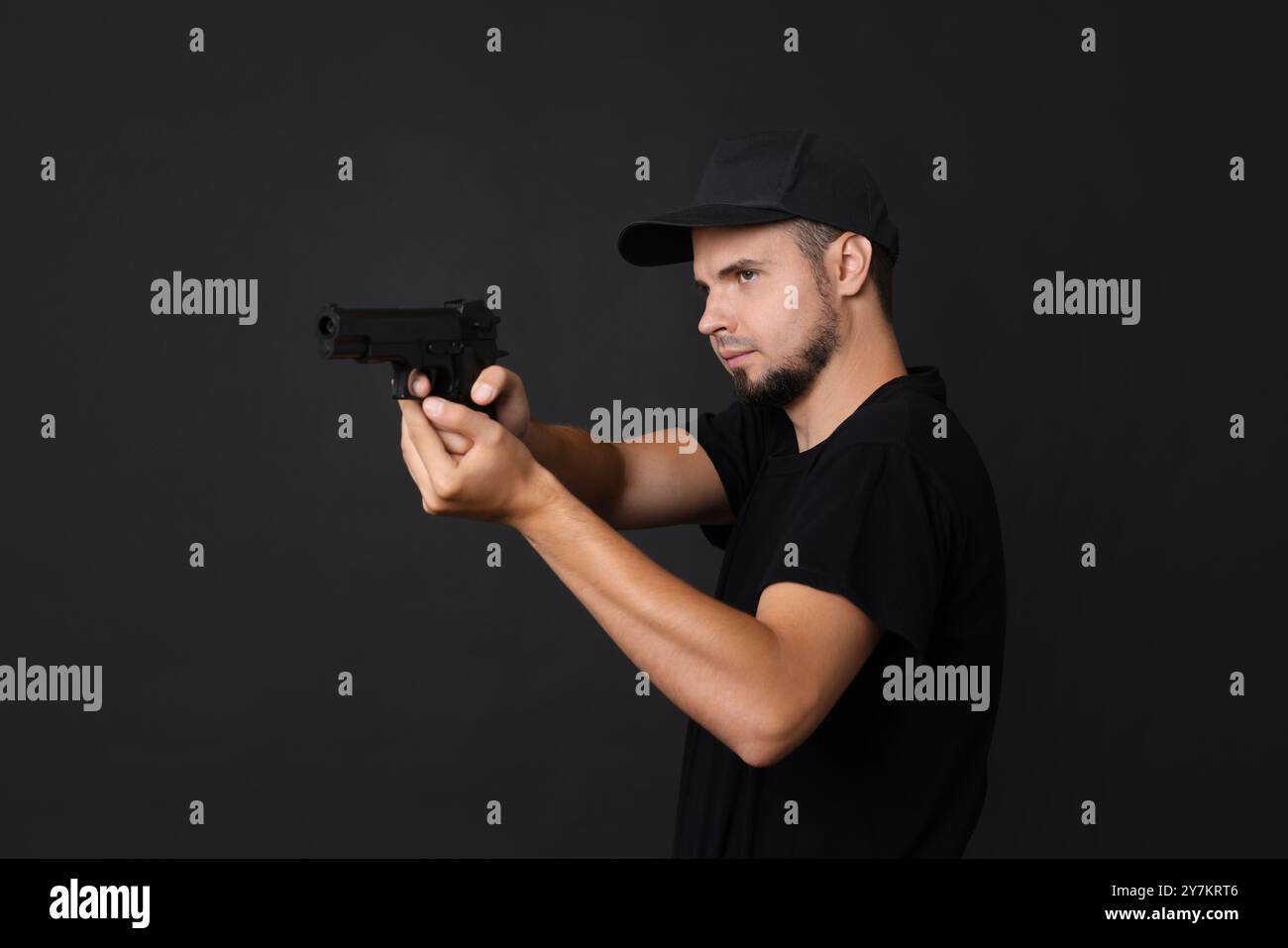 Young bodyguard using gun on black background Stock Photo - Alamy