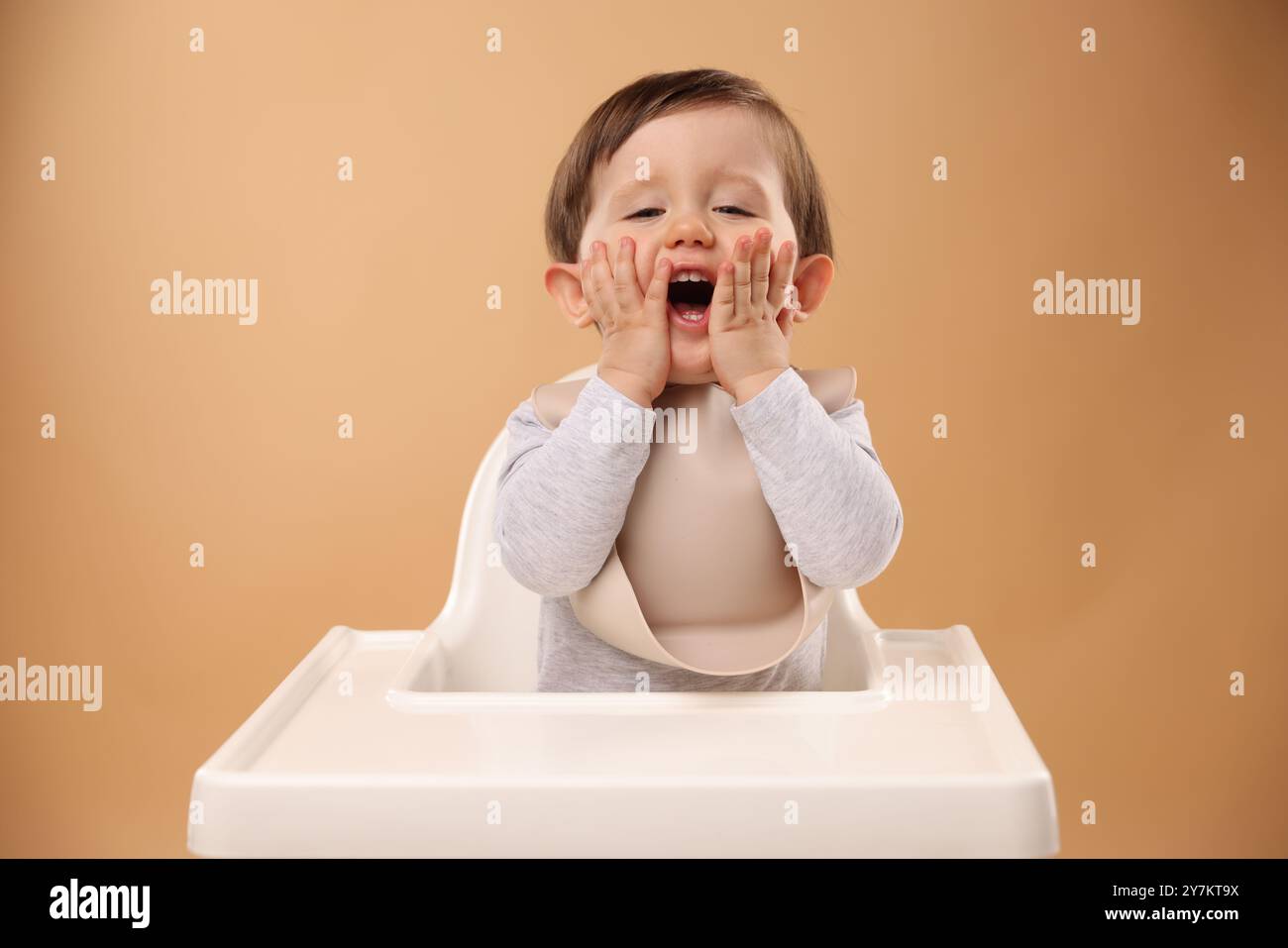 Cute little kid sitting in high chair on beige background Stock Photo ...