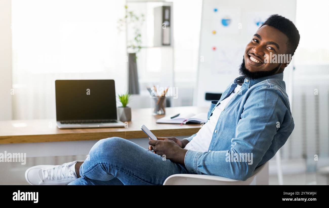Portrait of cheerful african american employee using smartphone at ...