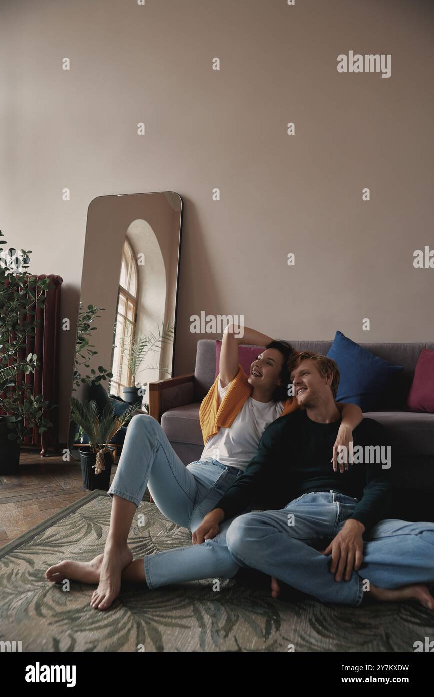 Dreamful young couple embracing and smiling while relaxing at home ...