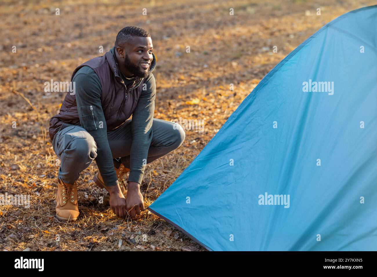 Black guy setting up blue tent in forest Stock Photo - Alamy