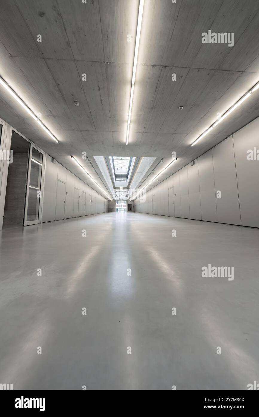 An elongated, well-lit corridor with concrete walls showing central ...