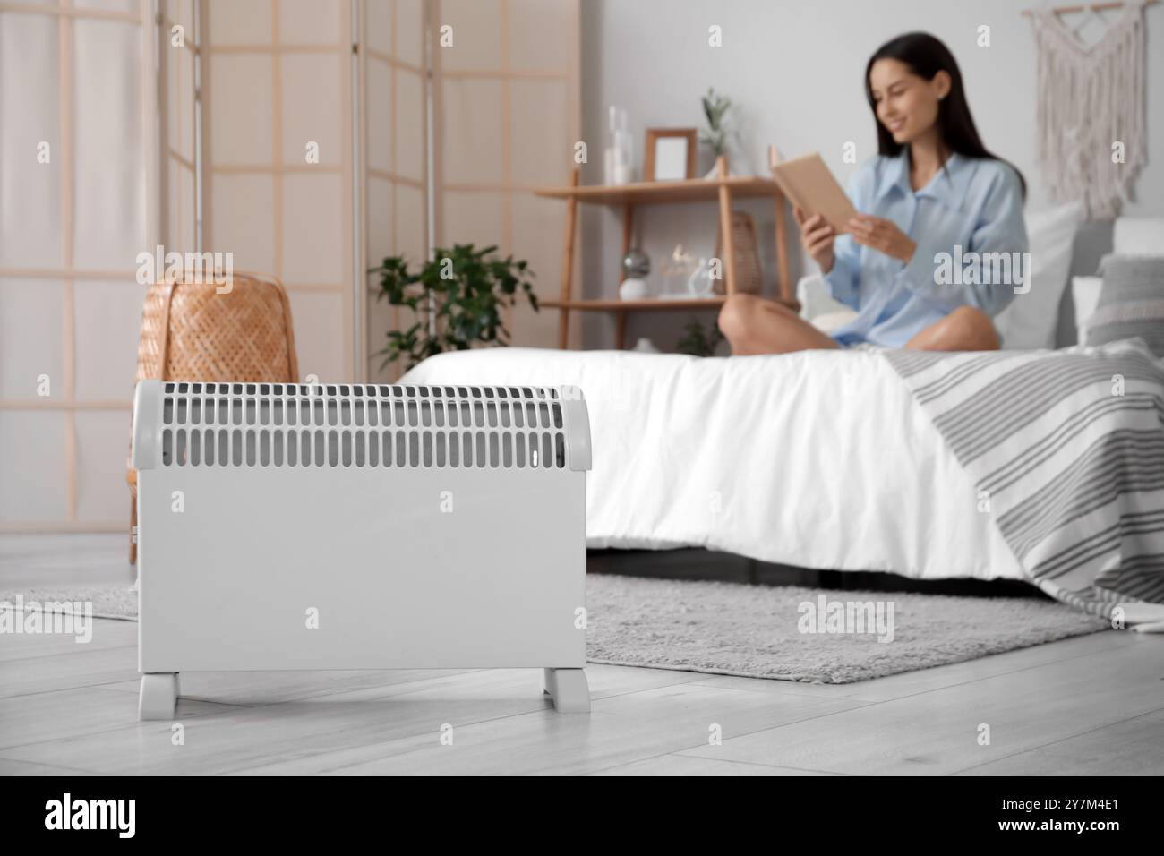 Electric heater on floor against young woman on bed in bedroom, closeup ...