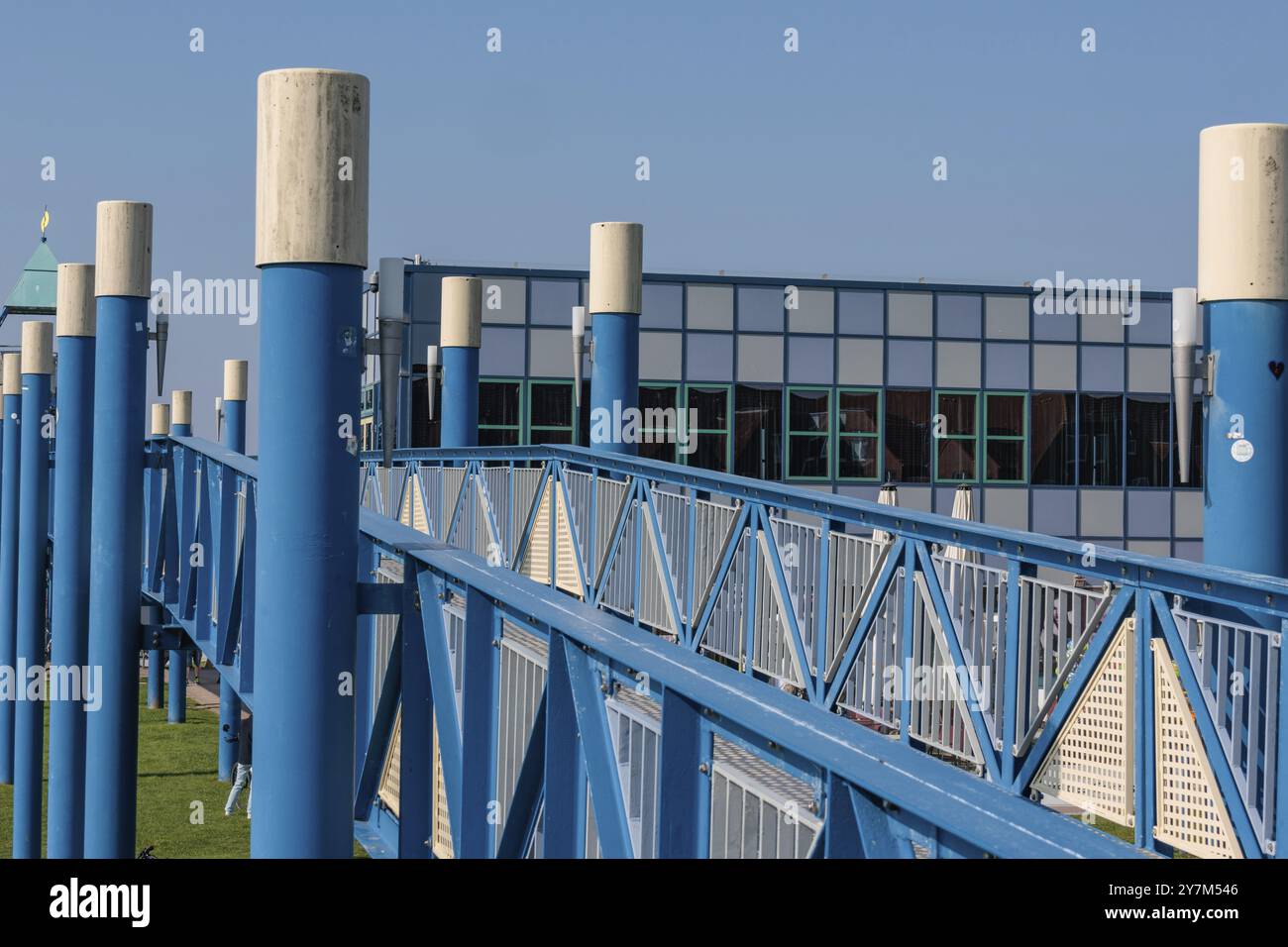 Blue footbridge leads to a modern building with large windows, clear ...