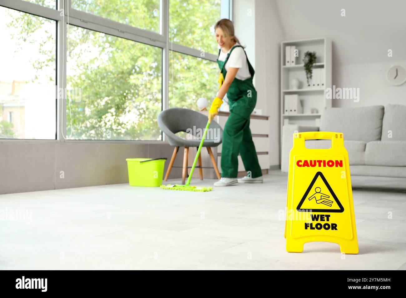 Caution sign against female janitor mopping floor in room, closeup ...
