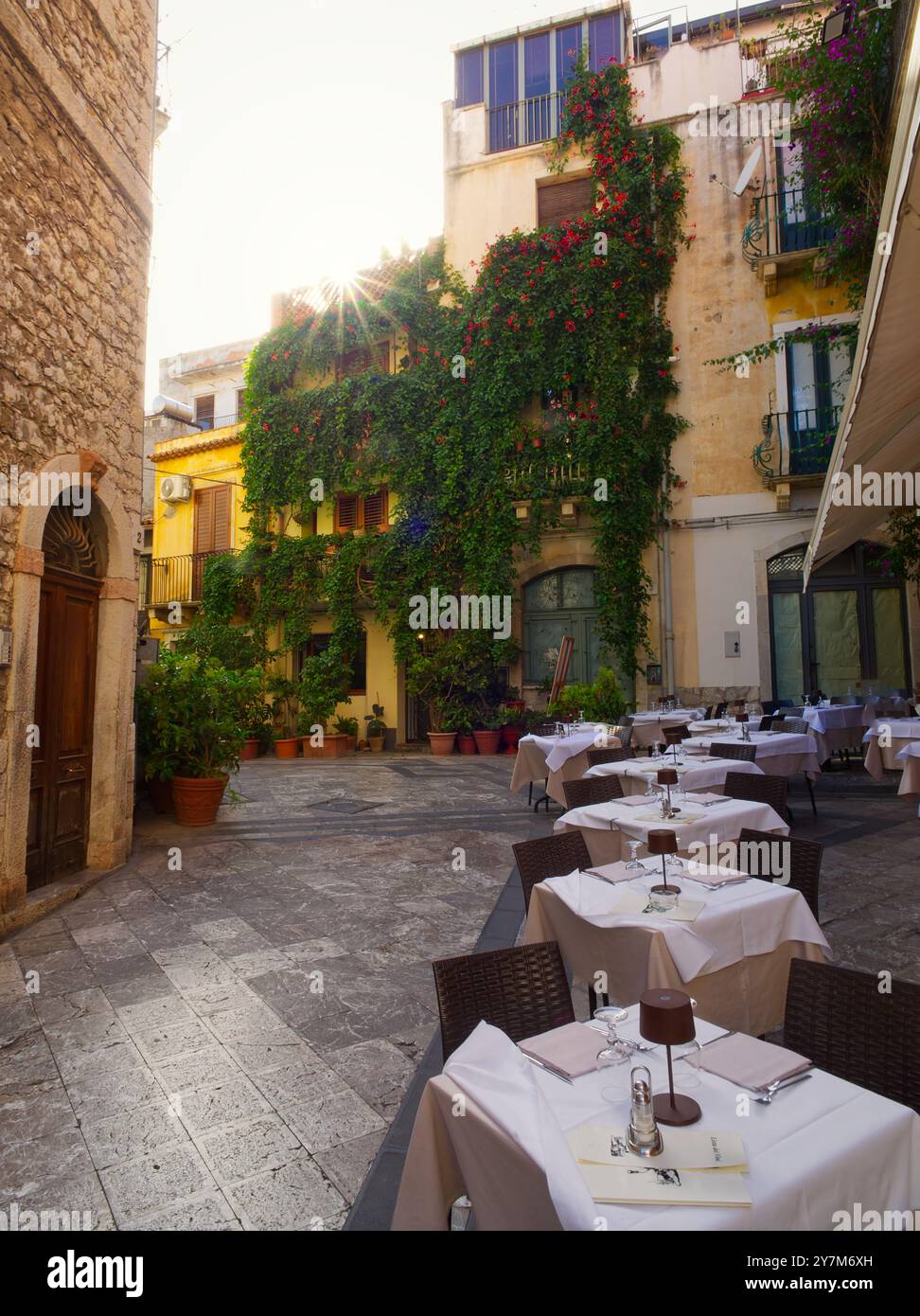 Taormina street and restaurant tables under sunbeam creating a sun star ...