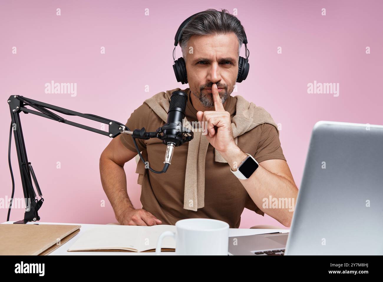 Serious mature man in headphones holding finger on lips while recording ...