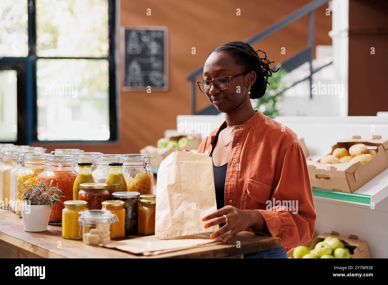 Black woman at wooden counter holding paper bag for putting fresh bio ...