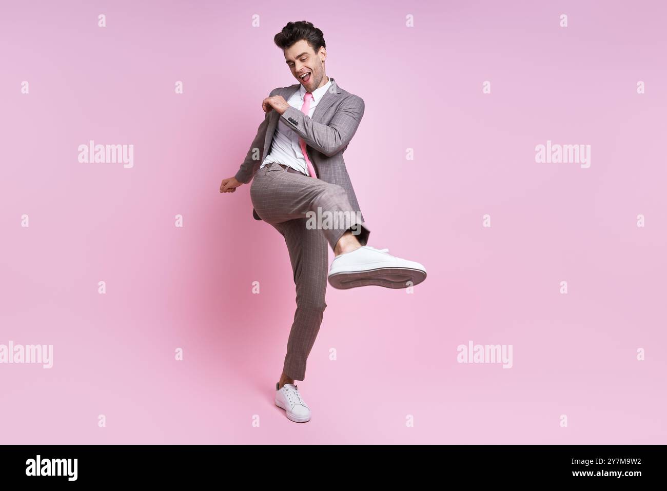 Happy young man in full suit throwing leg kick while standing against ...